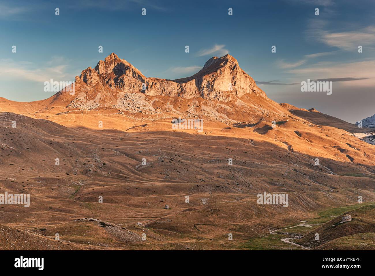 Warm sunlight illuminates the rocky slopes and peaks of two mountains ...