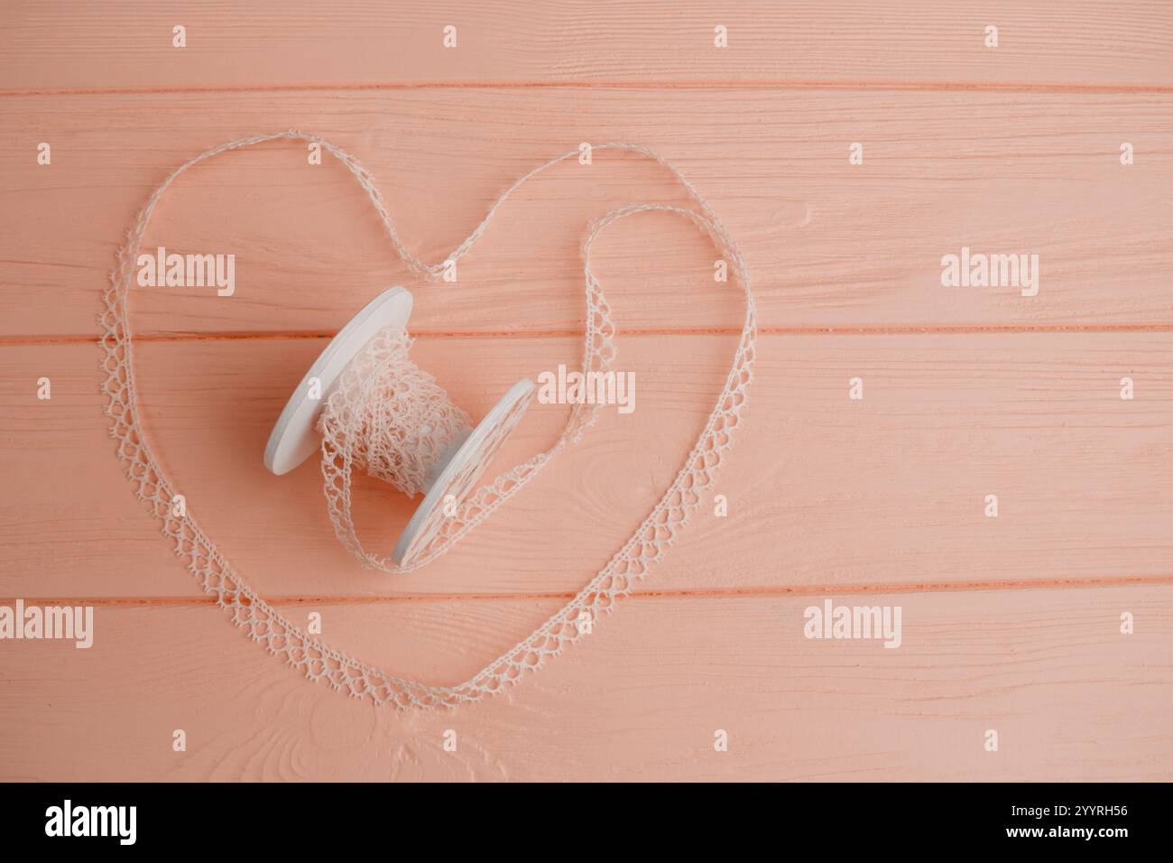 A vintage spool of soft pink lace is almost unwound and a heart-shaped ...