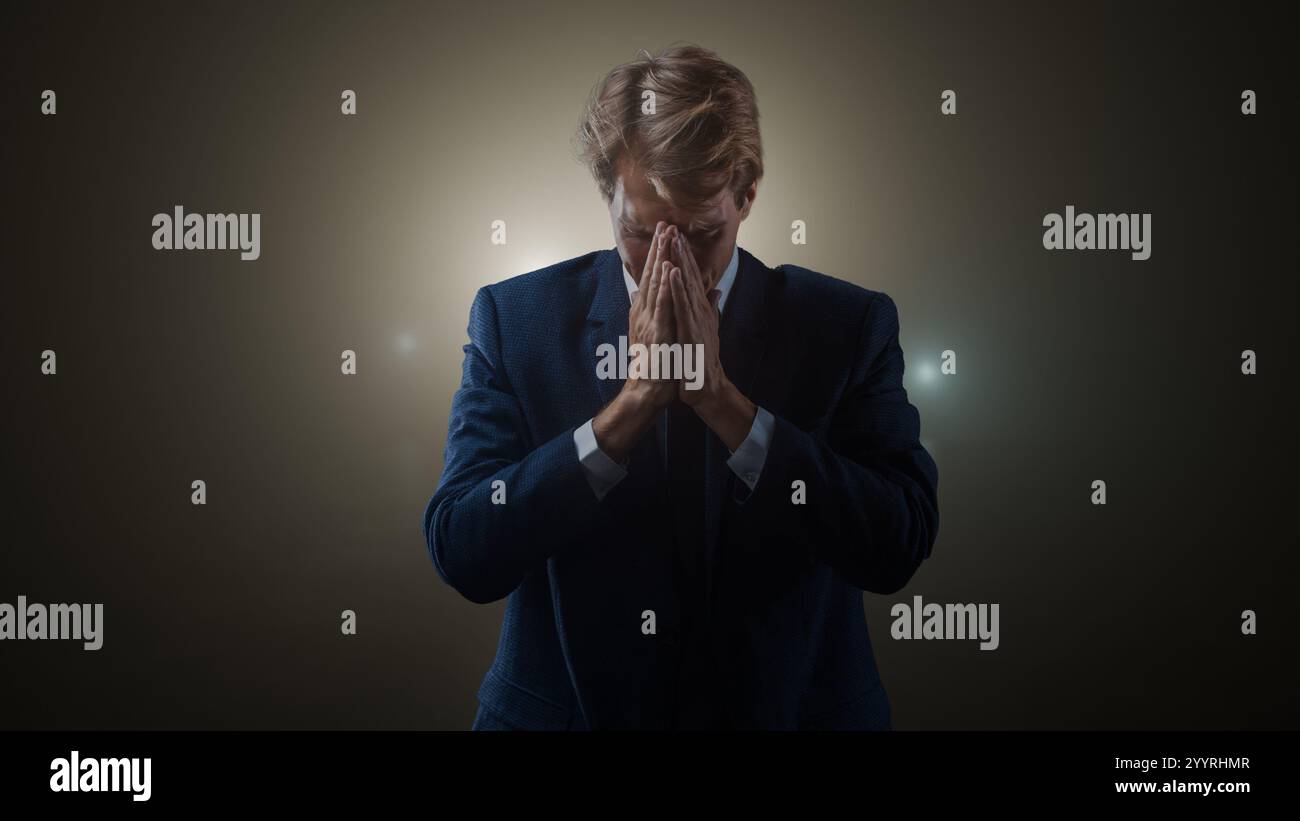 A young man in a business suit is stressed and covers his face with his ...
