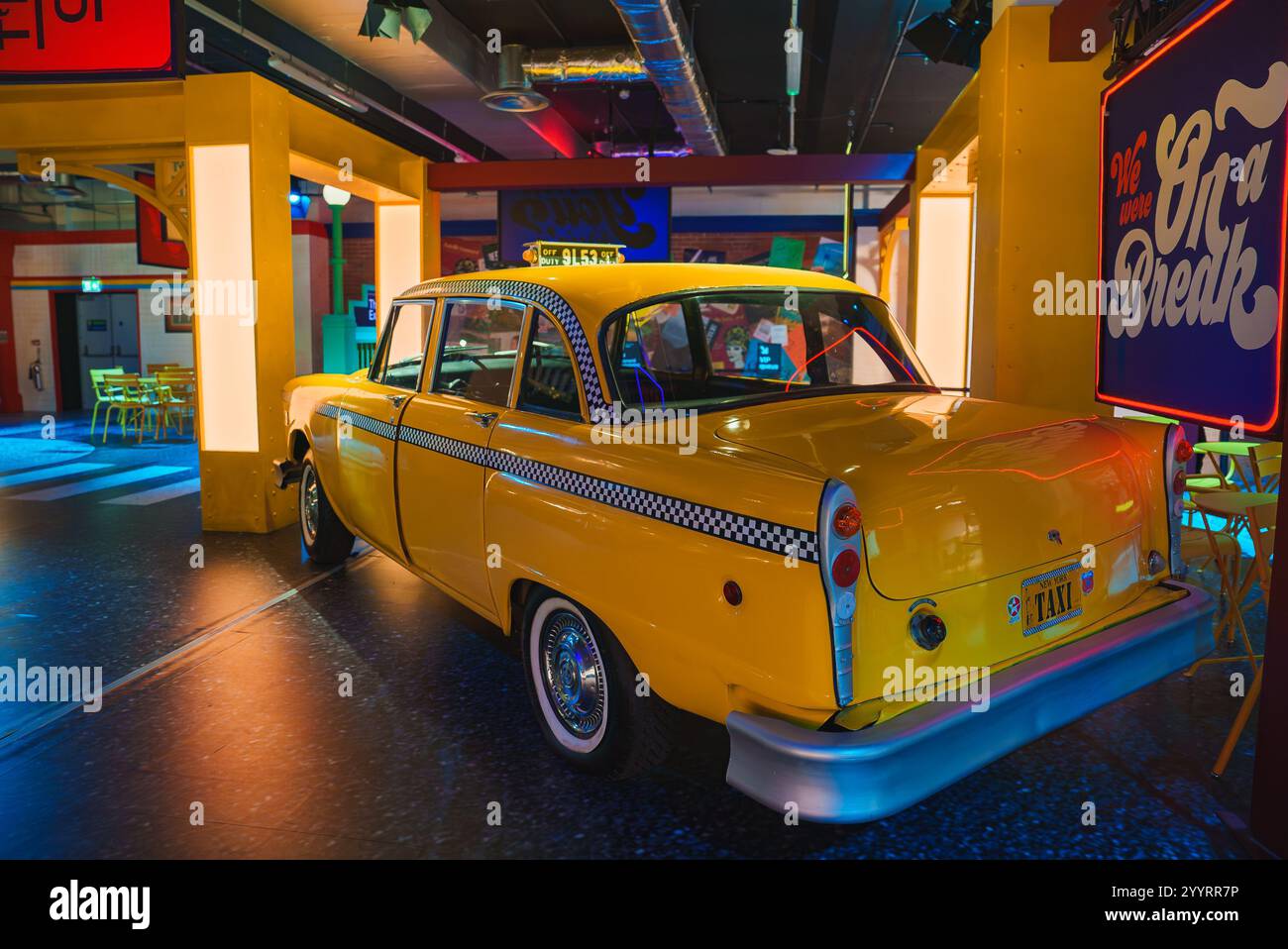 A classic yellow taxi cab is parked indoors amid vibrant lighting and ...