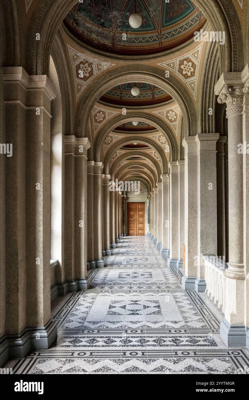 A long hallway with arched ceilings and a wooden door. The hallway is empty and the light is ...
