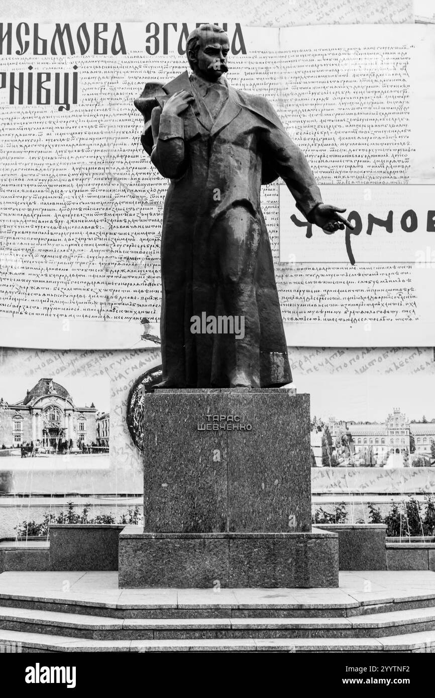 A statue of a man stands in front of a wall with writing on it. The ...