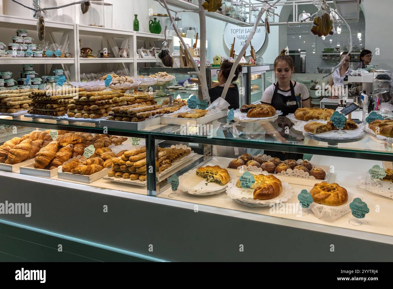 A bakery with a woman behind the counter. There are many pastries on ...