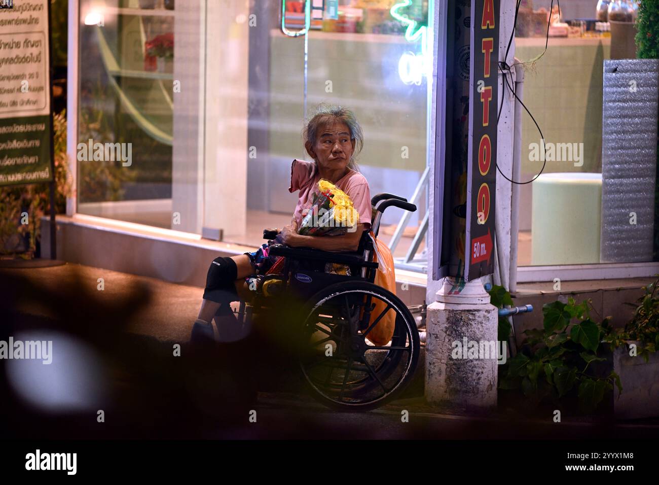An elderly Thai amputee lady sells flowers from her wheelchair in the ...