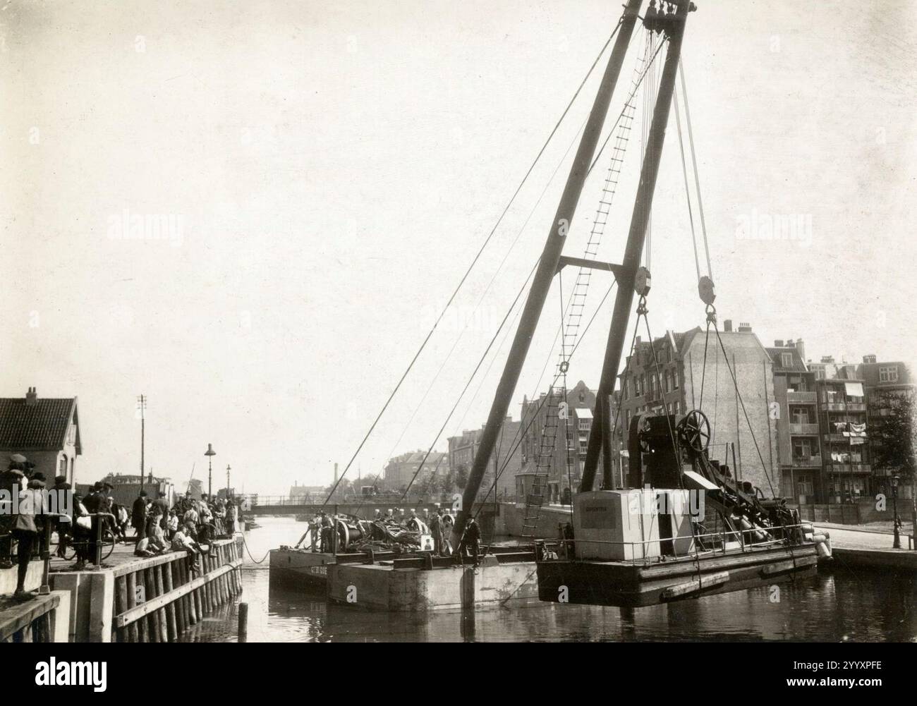 Een grote drijvende bok hijst een baggermolen over een gracht heen ...