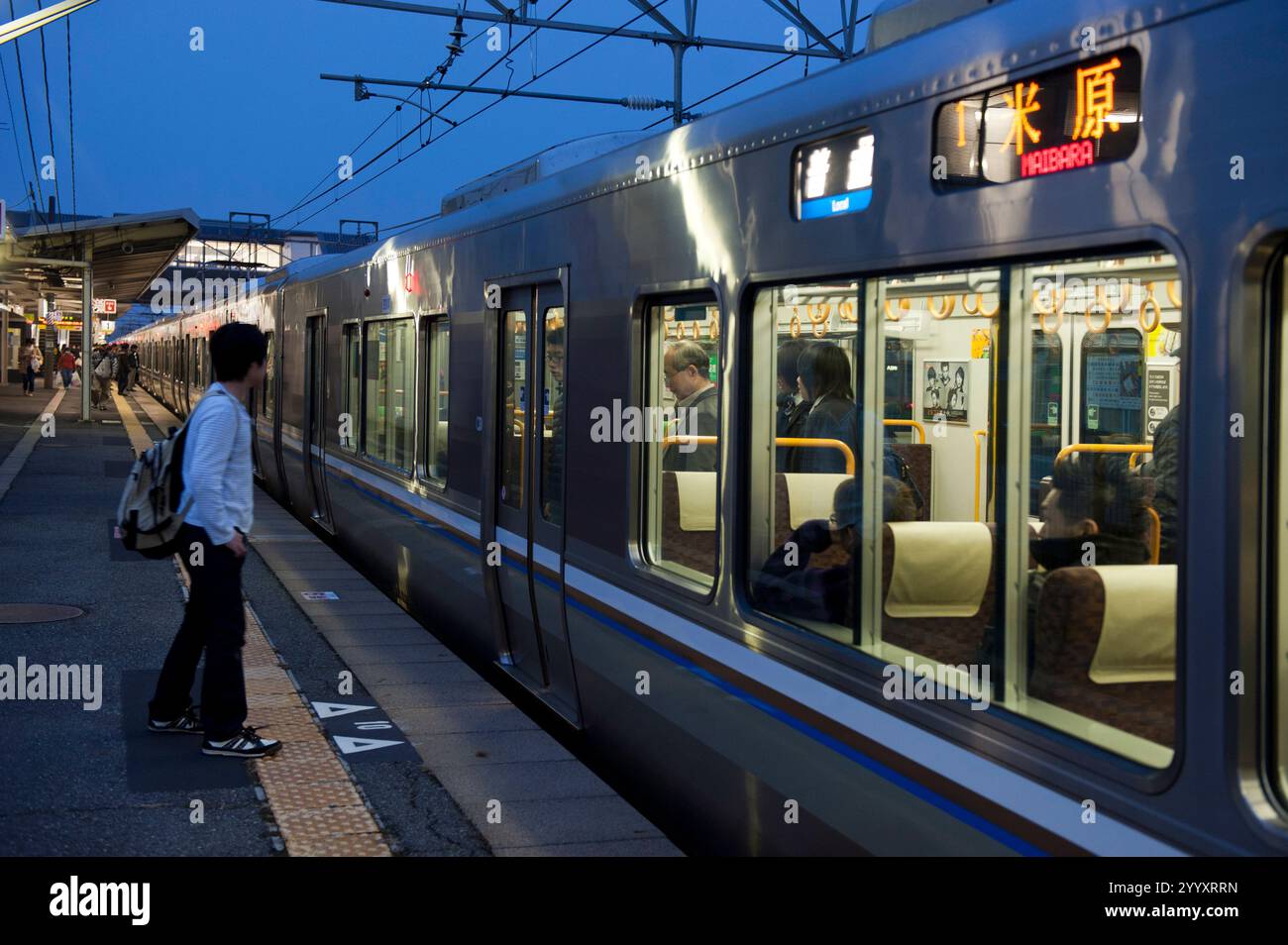 A passenger waits on a station platform to board an evening train on ...