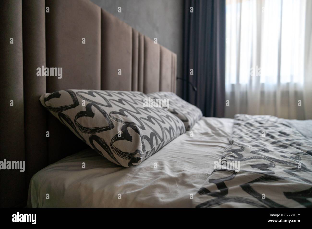 A bedroom with a bed featuring a padded headboard, two heart-patterned ...