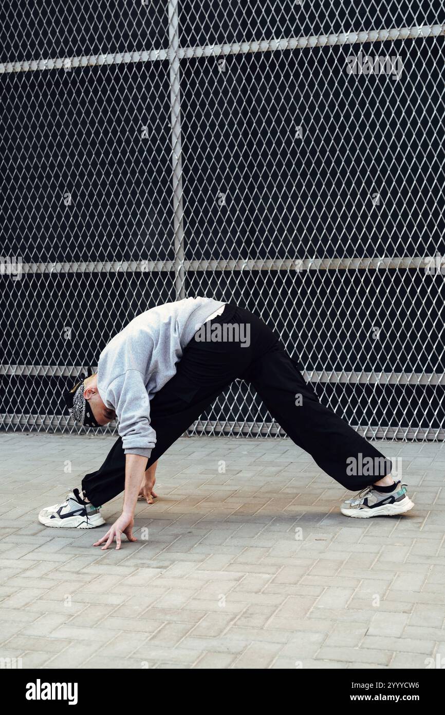 A person stretches in front of a chain link fence, reaching their hands ...