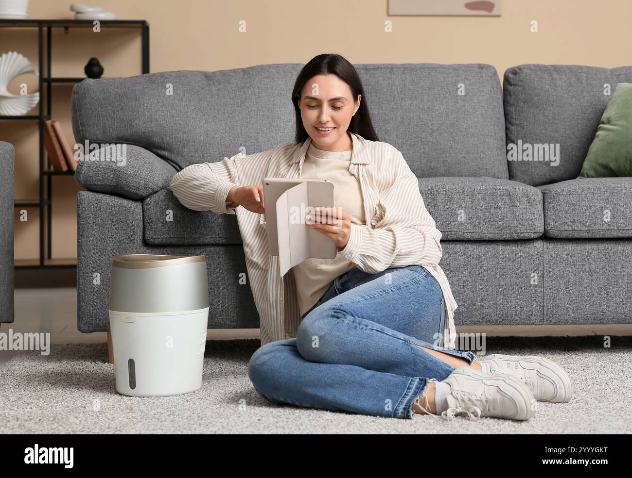 Beautiful young woman with modern air humidifier and tablet computer ...