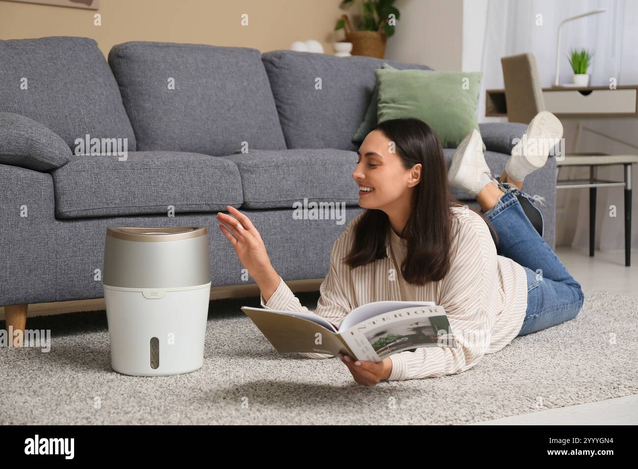 Beautiful young woman with modern air humidifier and magazine lying on ...