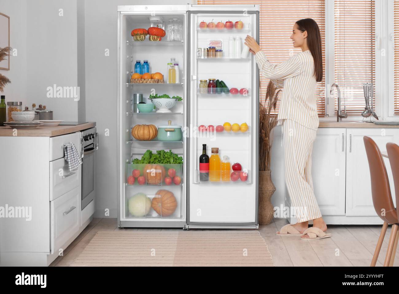 Young woman taking products from open fridge full of fresh food in ...