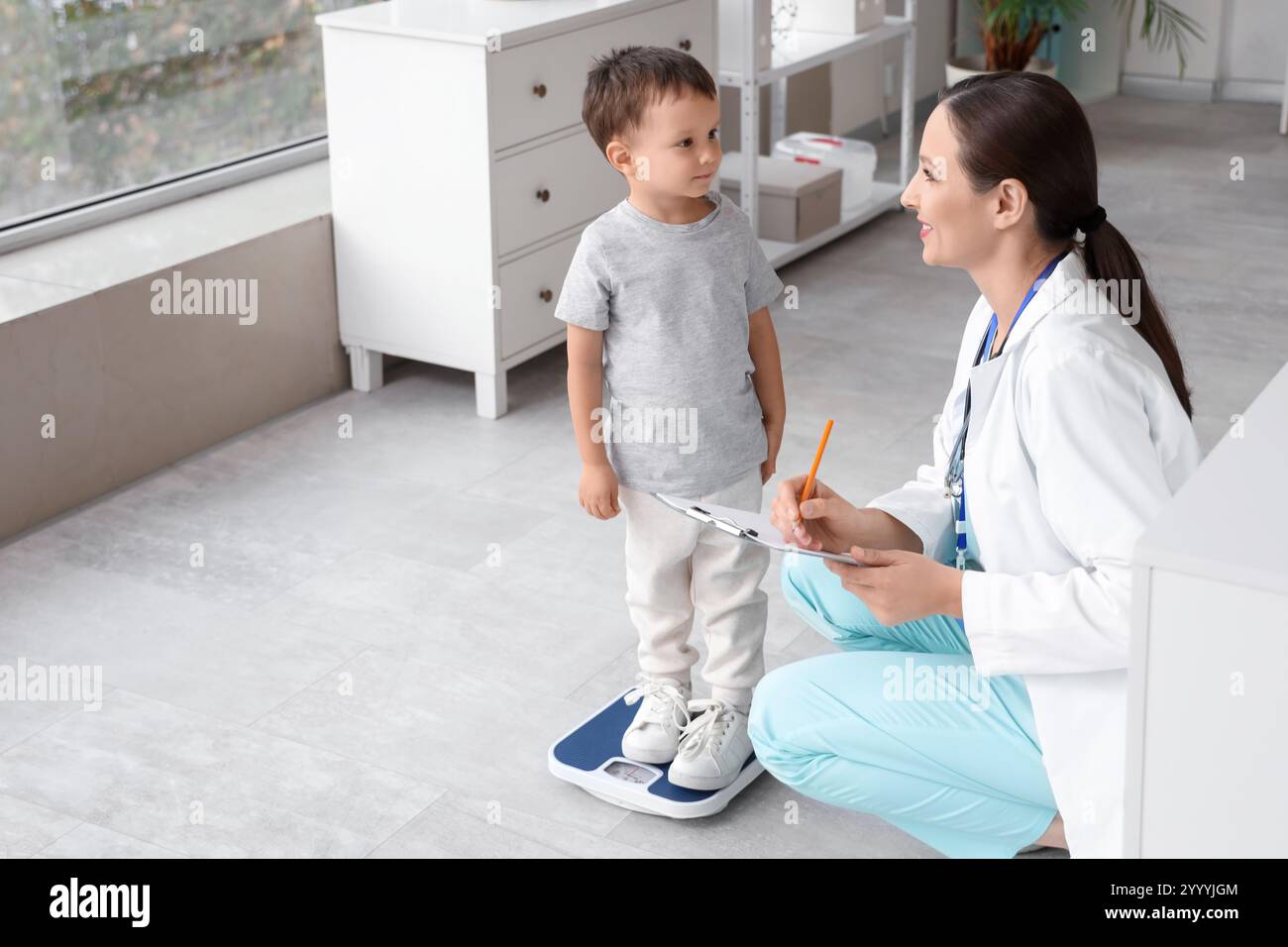 Female pediatrician with cute little boy measuring weight on scales in ...