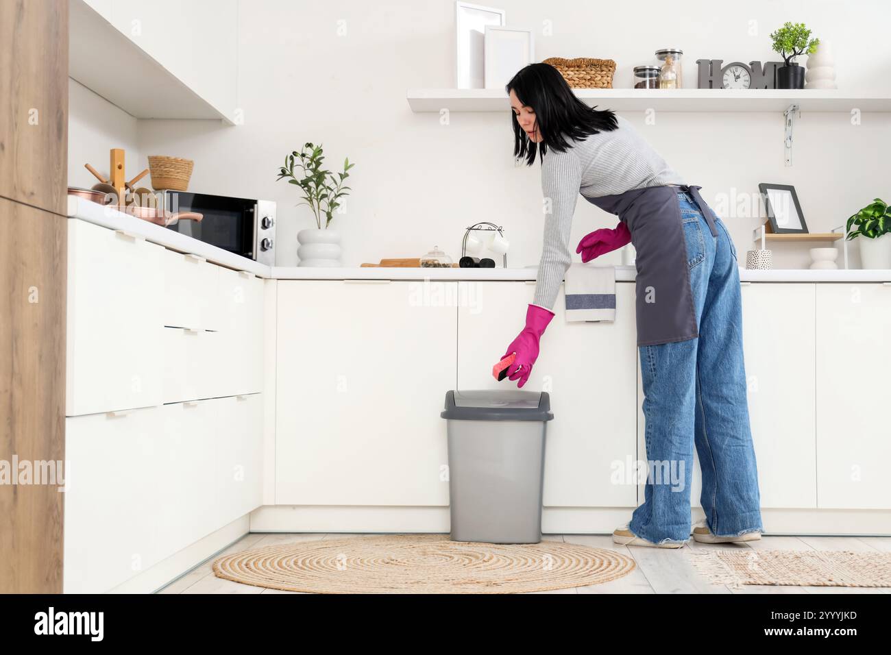 Beautiful young woman throwing used sponge into trash bin in kitchen ...