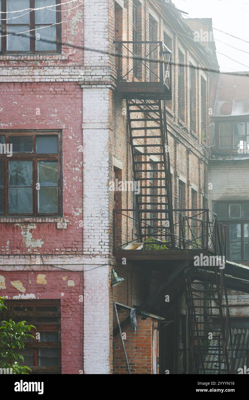 Old brick factory building with metal fire escape and peeling plaster ...