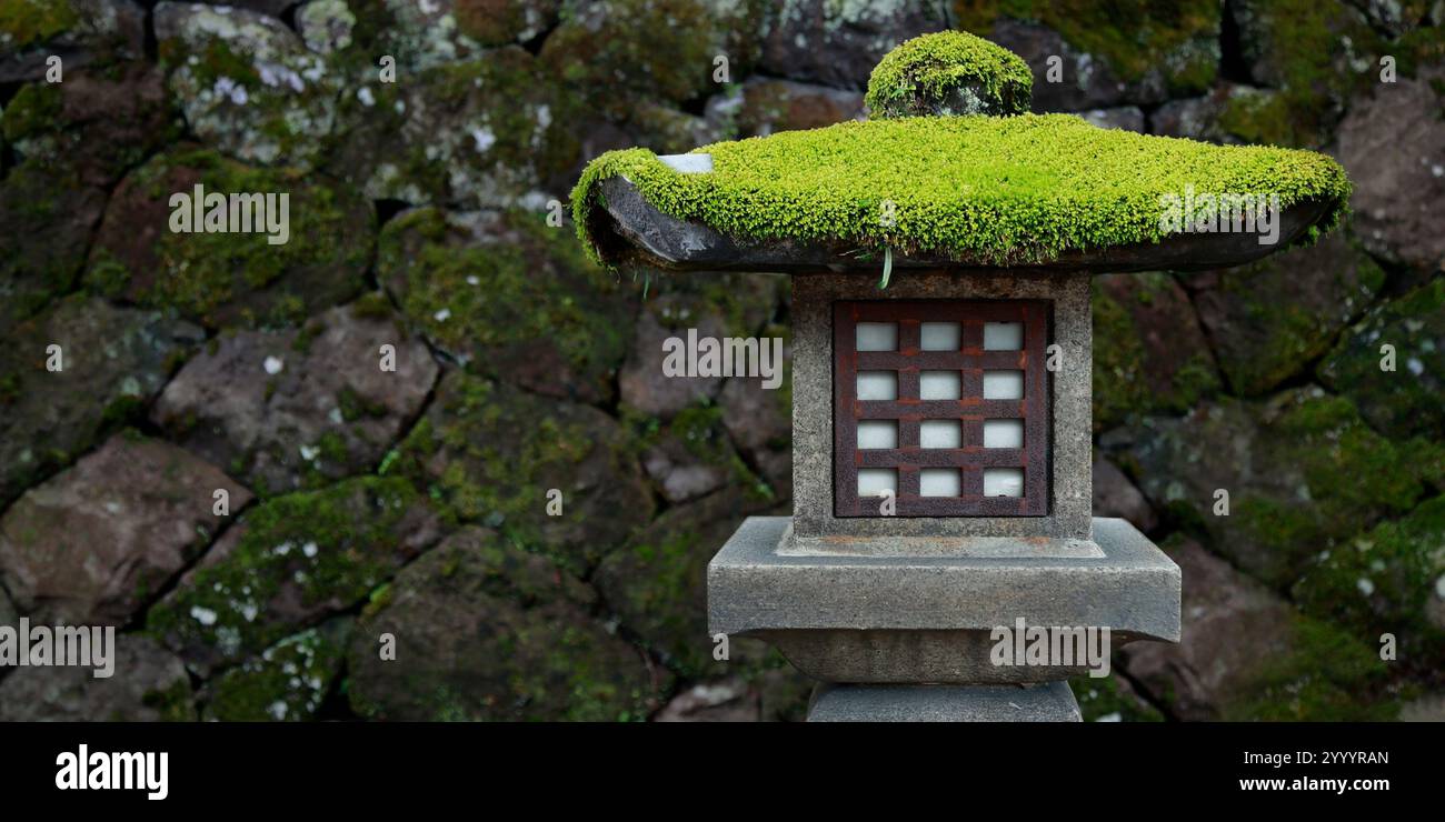 Traditional japanese stone lantern with moss in front of stone wall ...