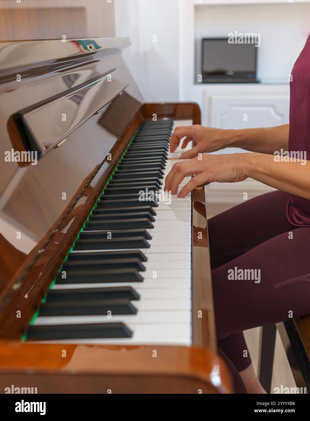 The photograph shows a wall-mounted piano from a side view, with the ...