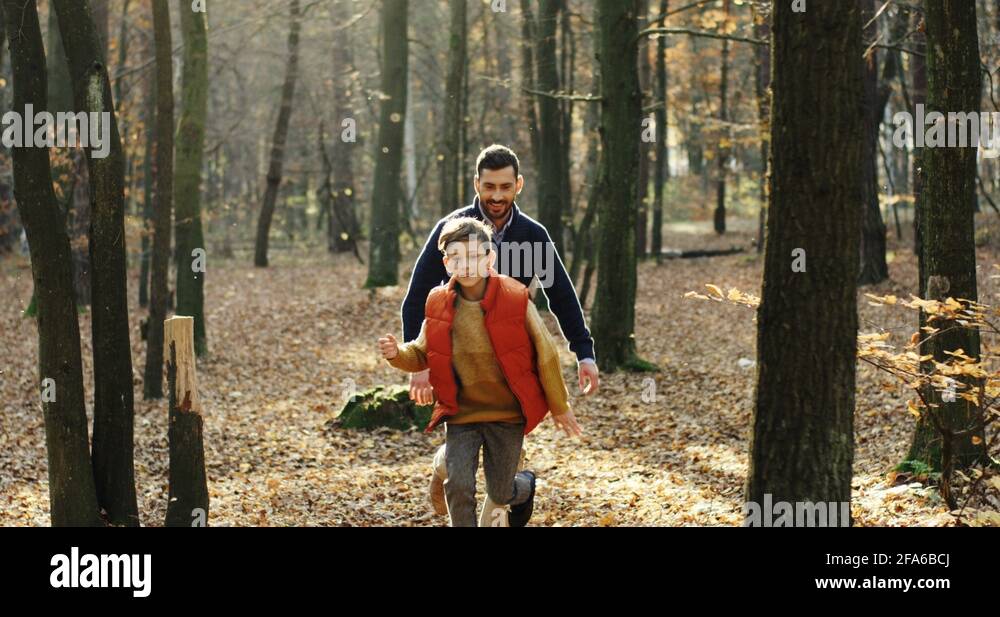 Cute small Caucasian boy running in the wood and his father following ...