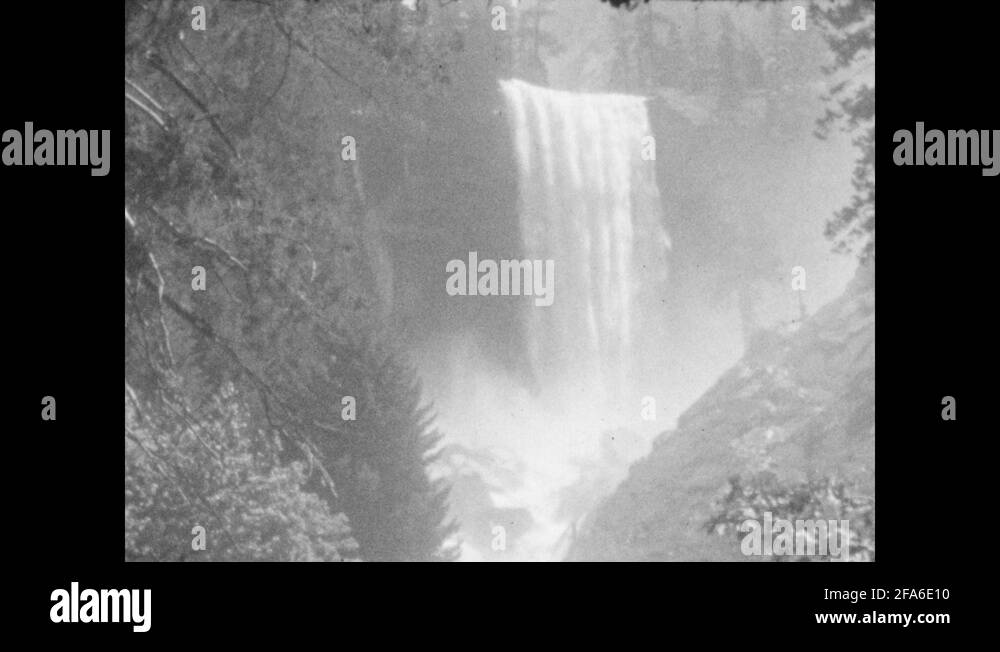 1940s: Waterfall. Man and boy scoot across log above river. Rushing ...