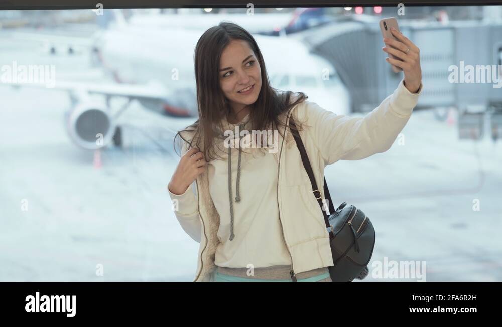 Beautiful woman makes selfie photo near airport window in background of ...