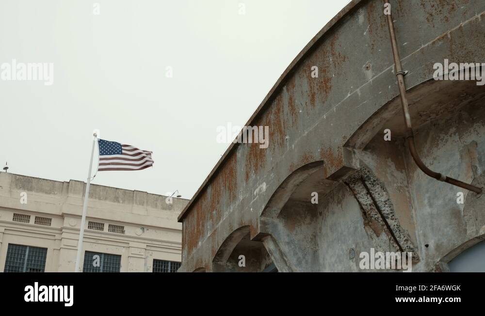 American flag on pole at Alcatraz island with concrete wall with arches ...