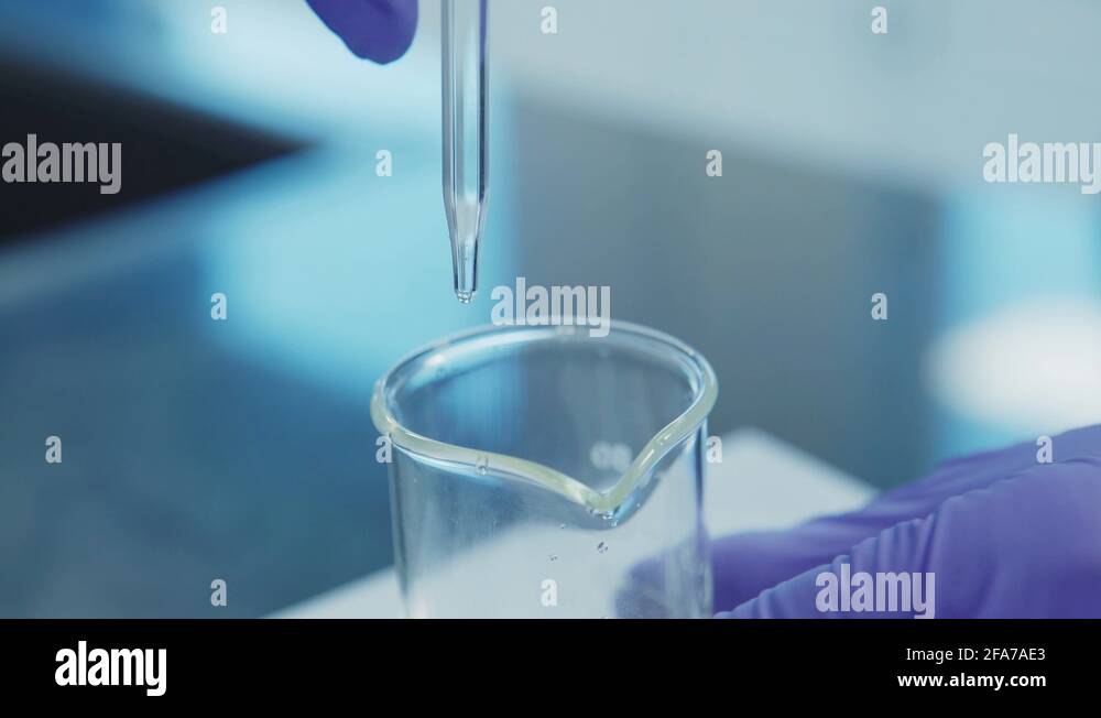 A scientist is pouring a chemical drop by drop in a beaker using a ...