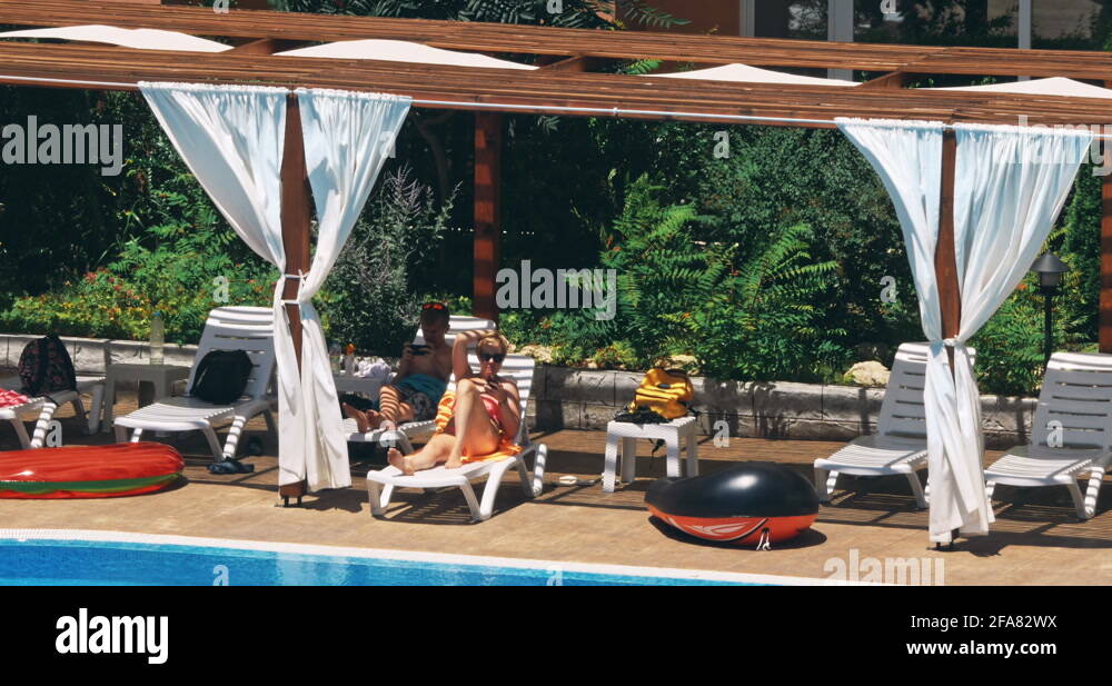 People sitting by the poolside of a resort swimming pool during summer ...