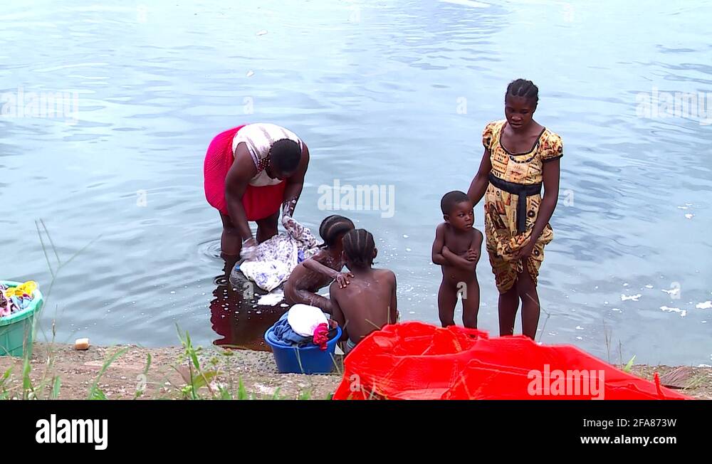 African woman washing her clothes and her children in a lake in ...