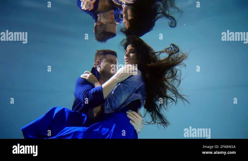 romantic loving couple are floating slowly underwater in large swimming ...