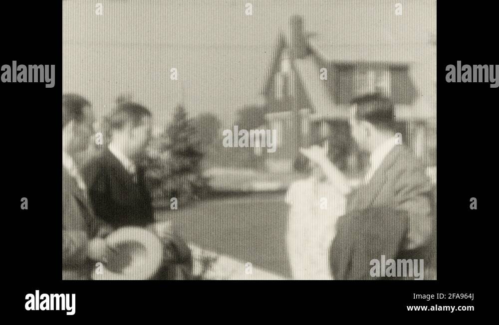 1920s: Yard, men talk, woman shields eyes from sun. Woman walks forward ...