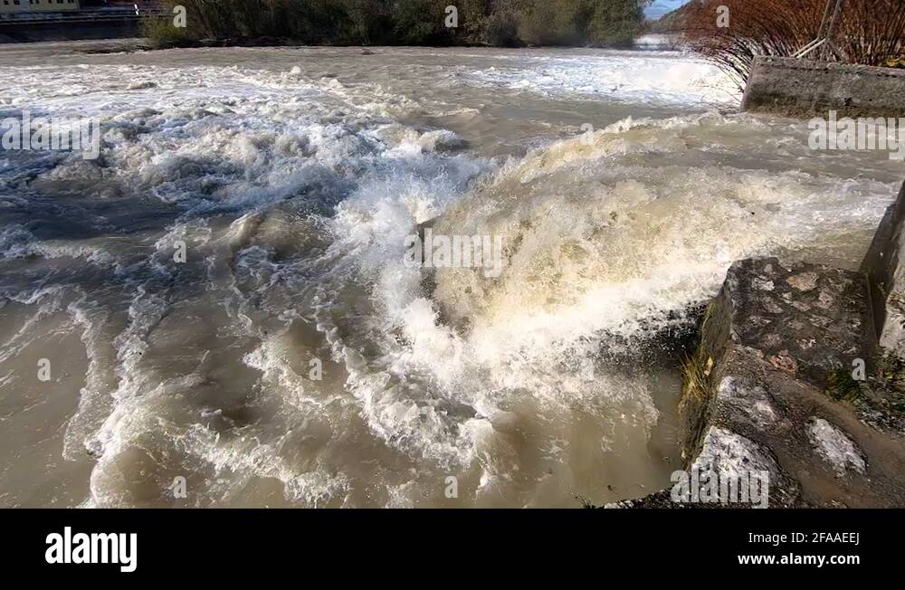 Dirty flood water flows from a man made wall with trees visible in the ...