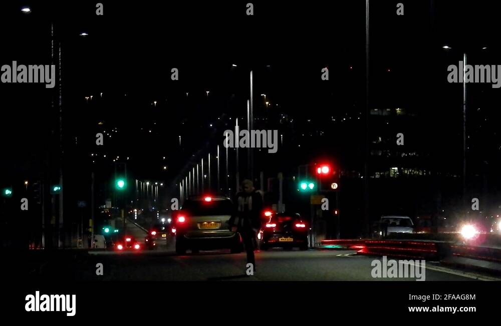 Night time city traffic scene. Male crossing road at beginning of shot ...