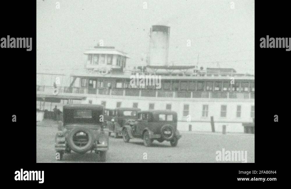 1920s: Car parked on dock. Boat anchored at dock. Boat steams across ...