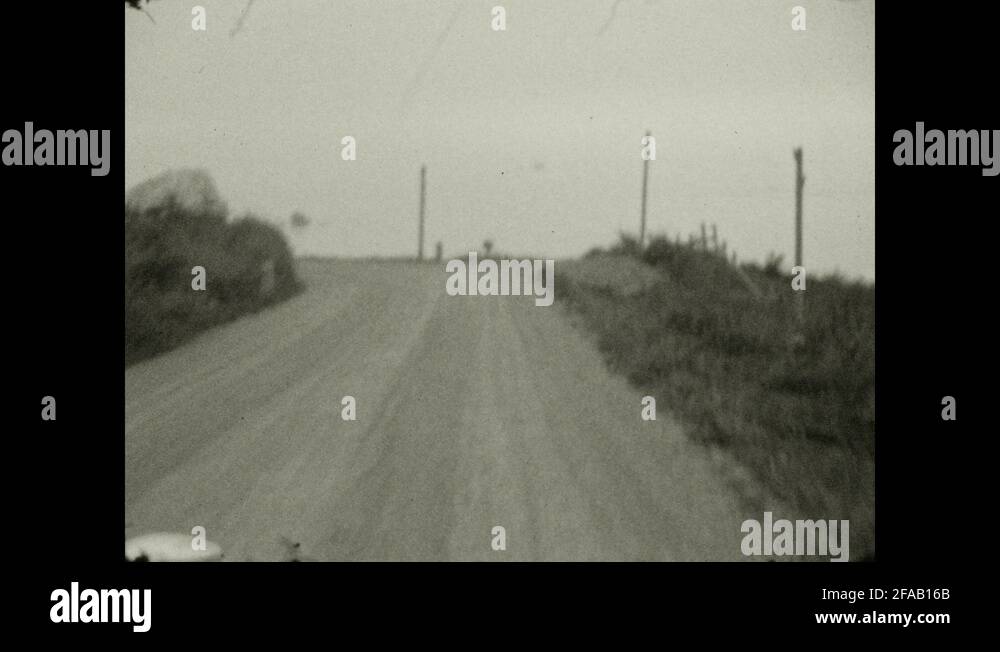 1920s: Cars drive down winding road and across bridge. Mountains. Beach ...