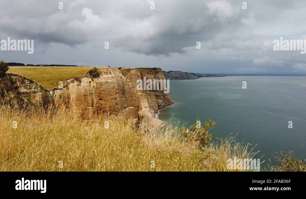 Sheer cliff face at Cape Kidnappers, New Zealand. Storm clouds on ...