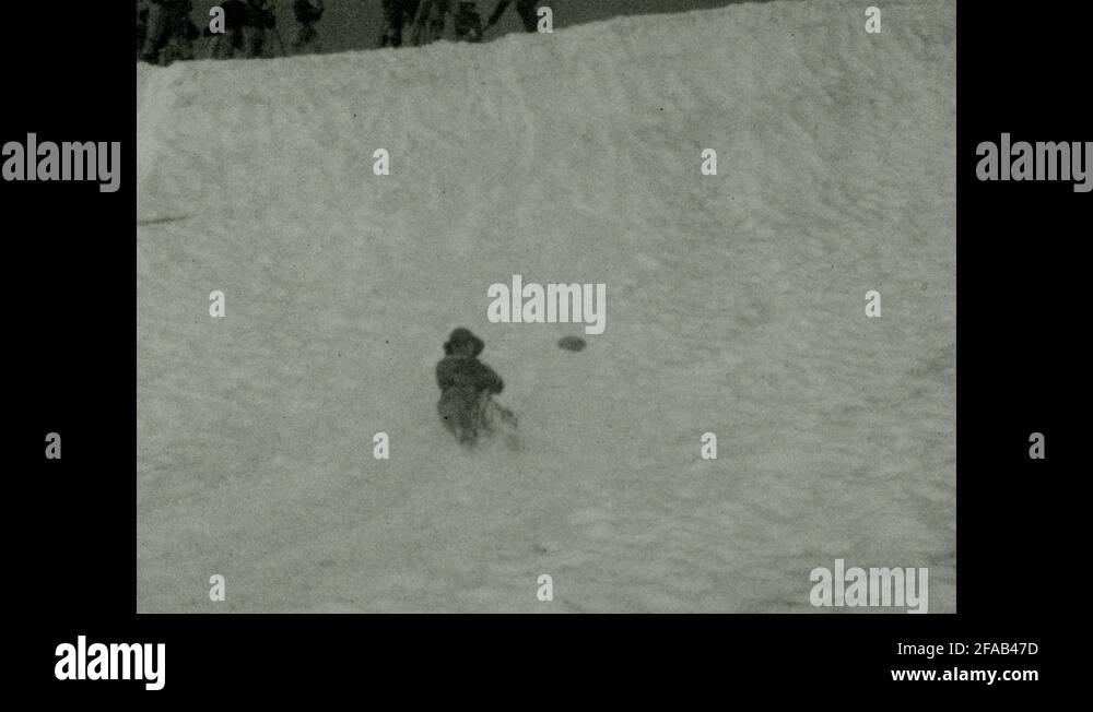 1930s: UNITED STATES: man slides down snow slope. Lady slides down snow ...