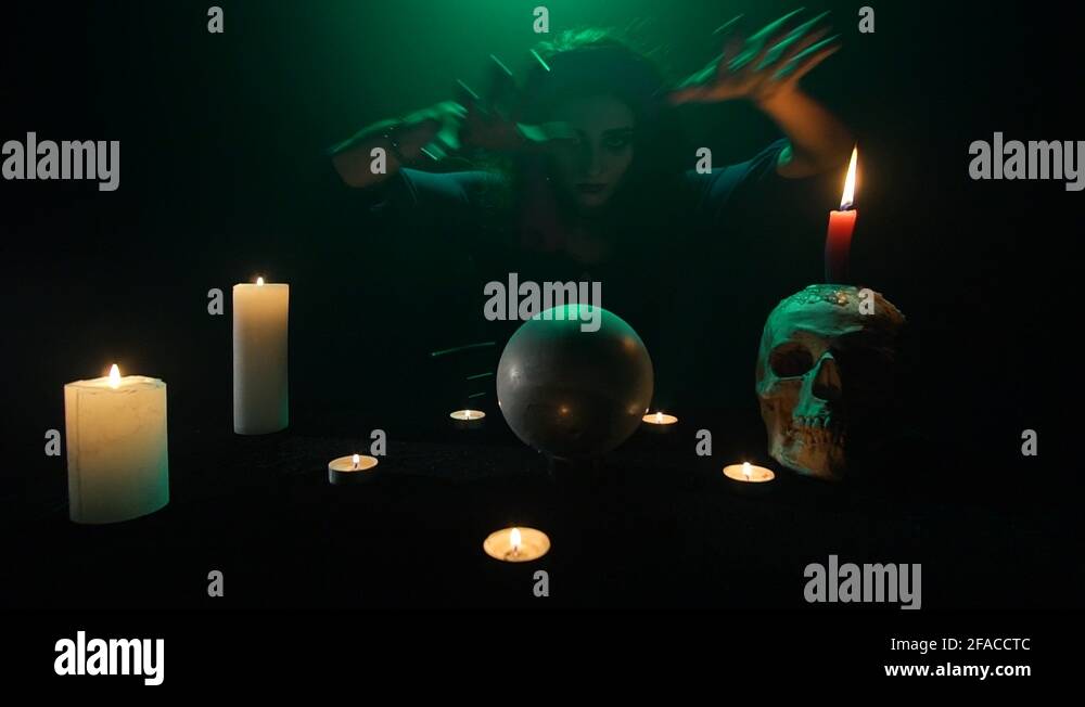 Scary occultist woman conjuring on a crystal ball, table with candles ...