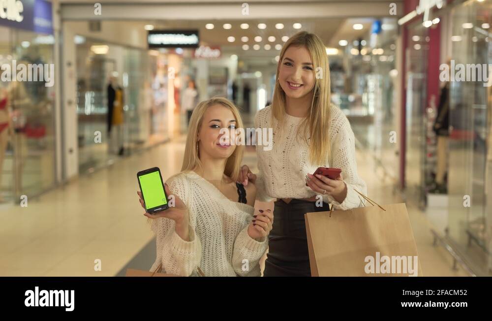 Two stylish, blondie girls are in shopping mall. They are standing ...
