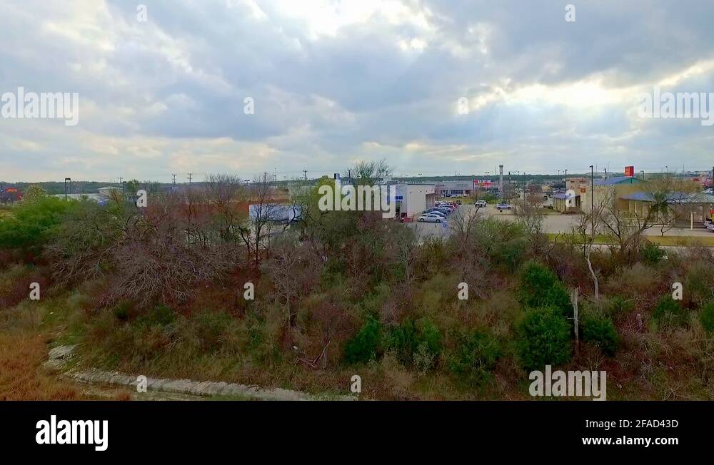 Drone footage Rise from below tree line to reveal shops car parks and ...