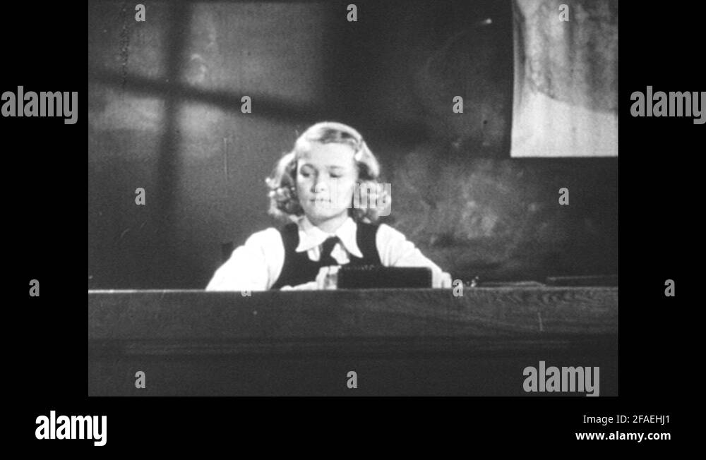 1950s: Girl sits at teacher's desk in classroom. She grabs books and ...