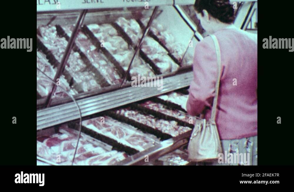 1970s: Woman grocery shopping. Meat on shelf. Man stalking shelves ...