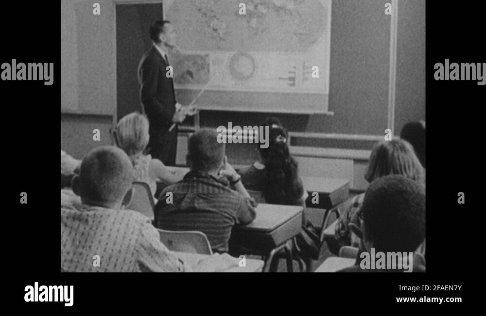 1960s: Teacher pulls down world map and uses pointer. Children listen ...