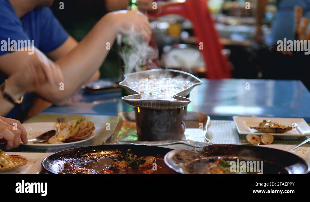 Close up shot across table of people eating steaming variety of foods ...