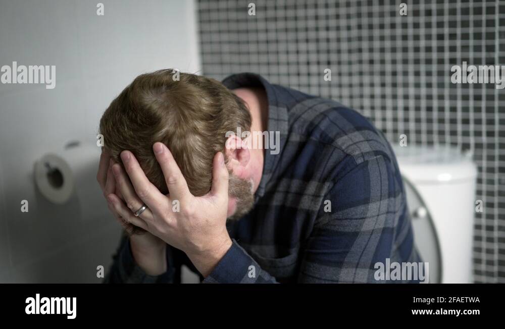 Constipated man sits on toilet with his head in hands, suffering in ...