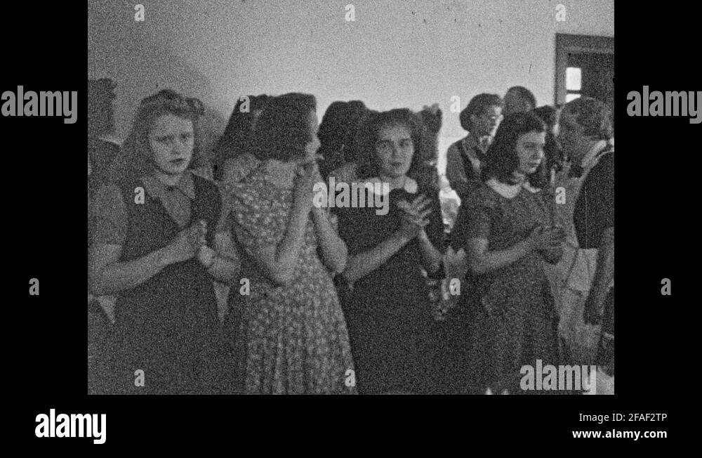 1930s: Young girls stand at table with hands clasped. Line of girl ...