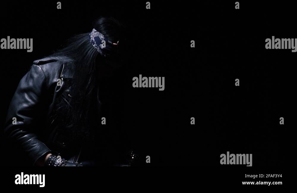 A rocker sitting in the dark and showing the sign of the horns with two ...