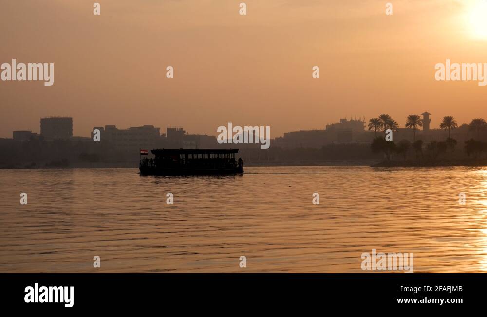 A ferry crossing the Nile River flying the Egyptian flag at sunset ...