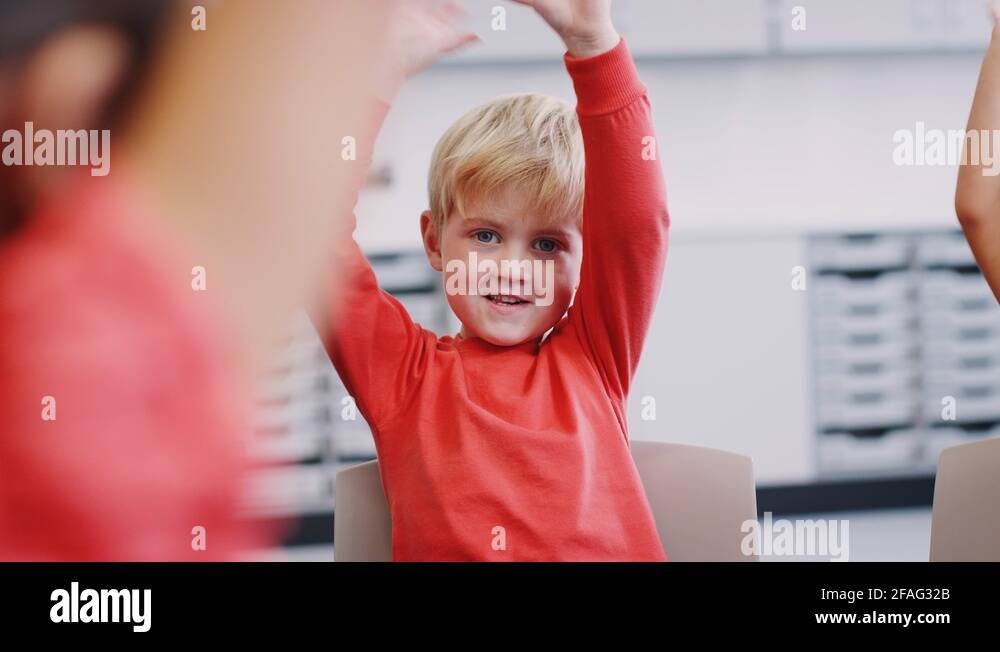 Infant schoolchildren waving their arms in the air and clapping during ...