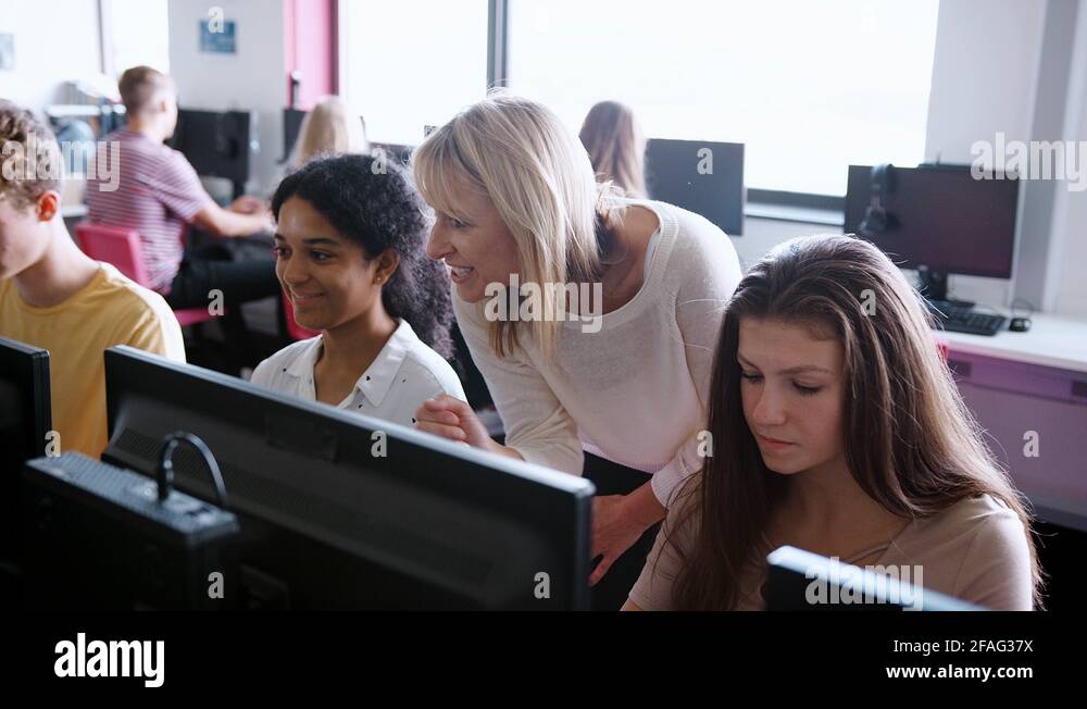 Female Teacher Helping Teenage High School Students Working In Computer ...