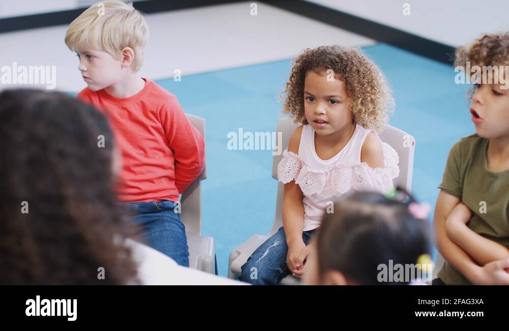 Infant school kids sitting on chairs in classroom listening to their ...
