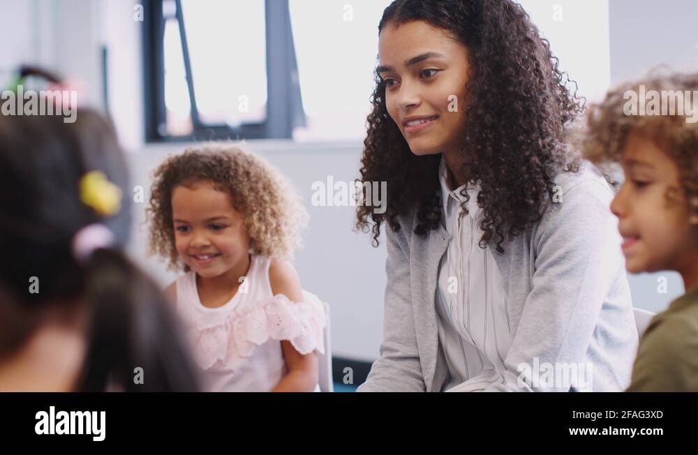 Infant school children sitting on chairs in a classroom talking with ...